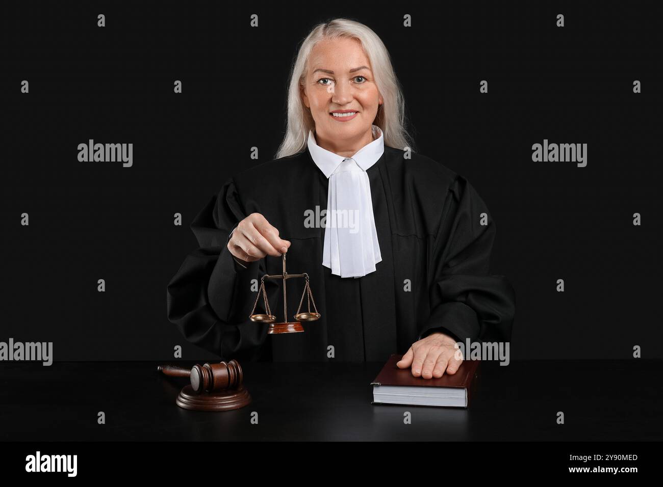 Mature female judge with scales of justice and book at table on black ...