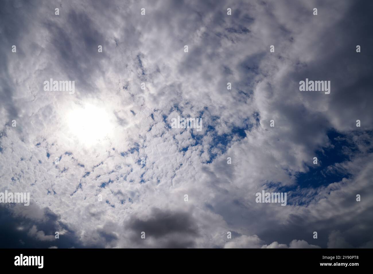 A dramatic sky with thick clouds partially covering the sun, creating a ...