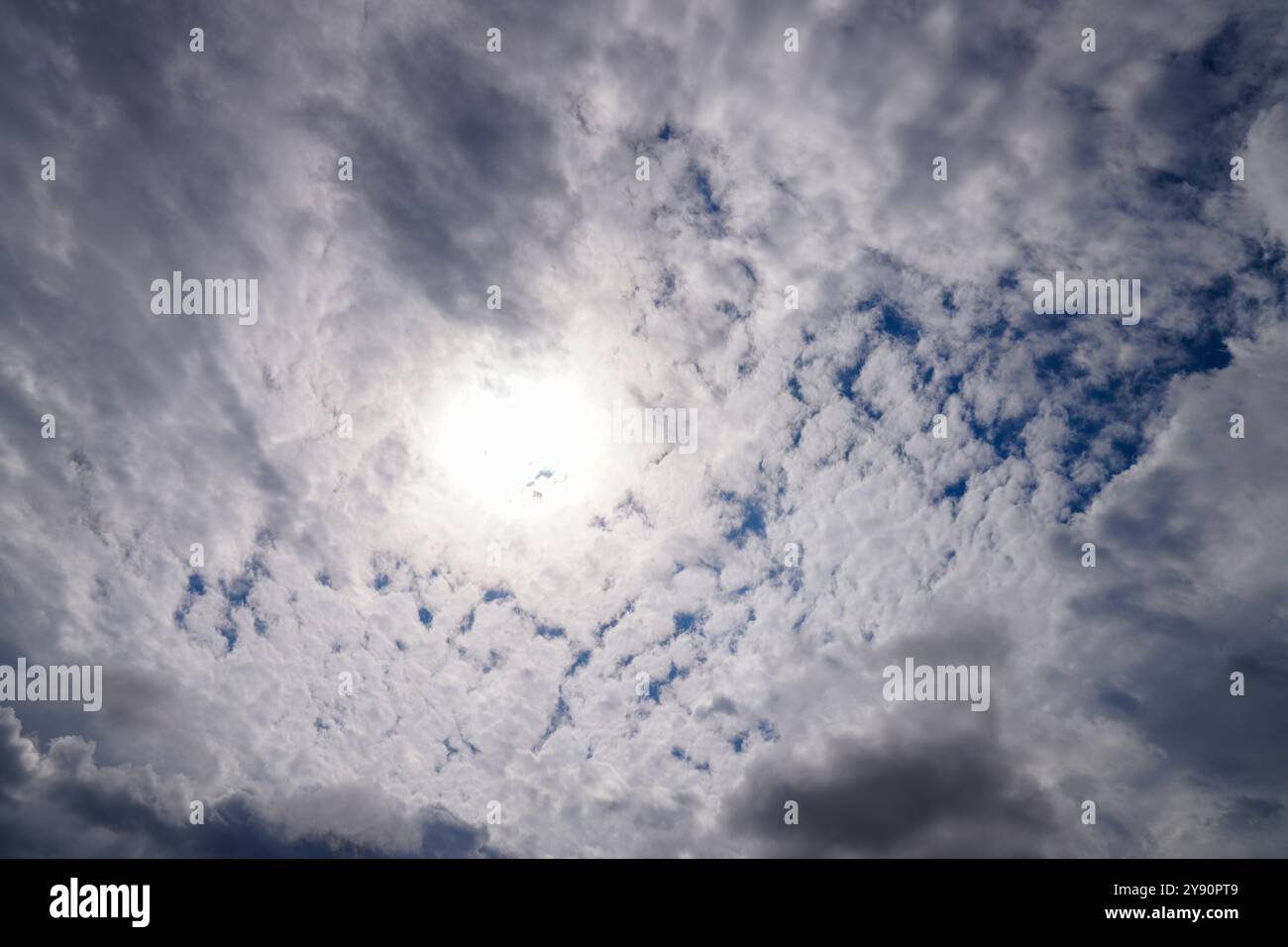 A dramatic sky with thick clouds partially covering the sun, creating a ...
