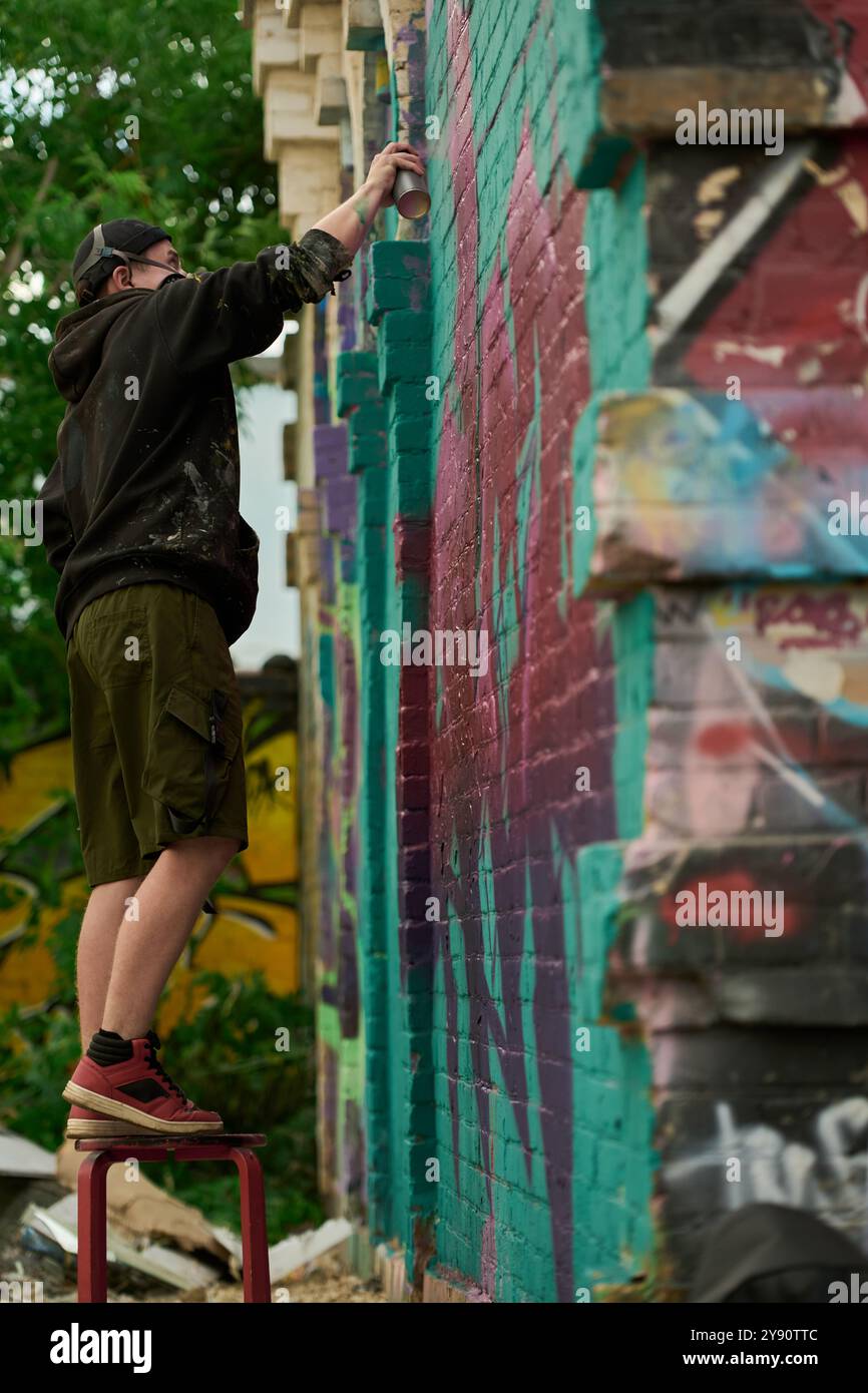 Side view of young man in respirator standing on stool in front of wall ...