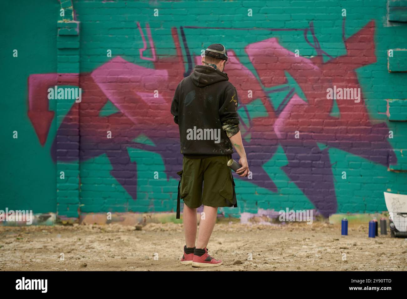 Back view of young creative graffiti artist with can of paint looking ...
