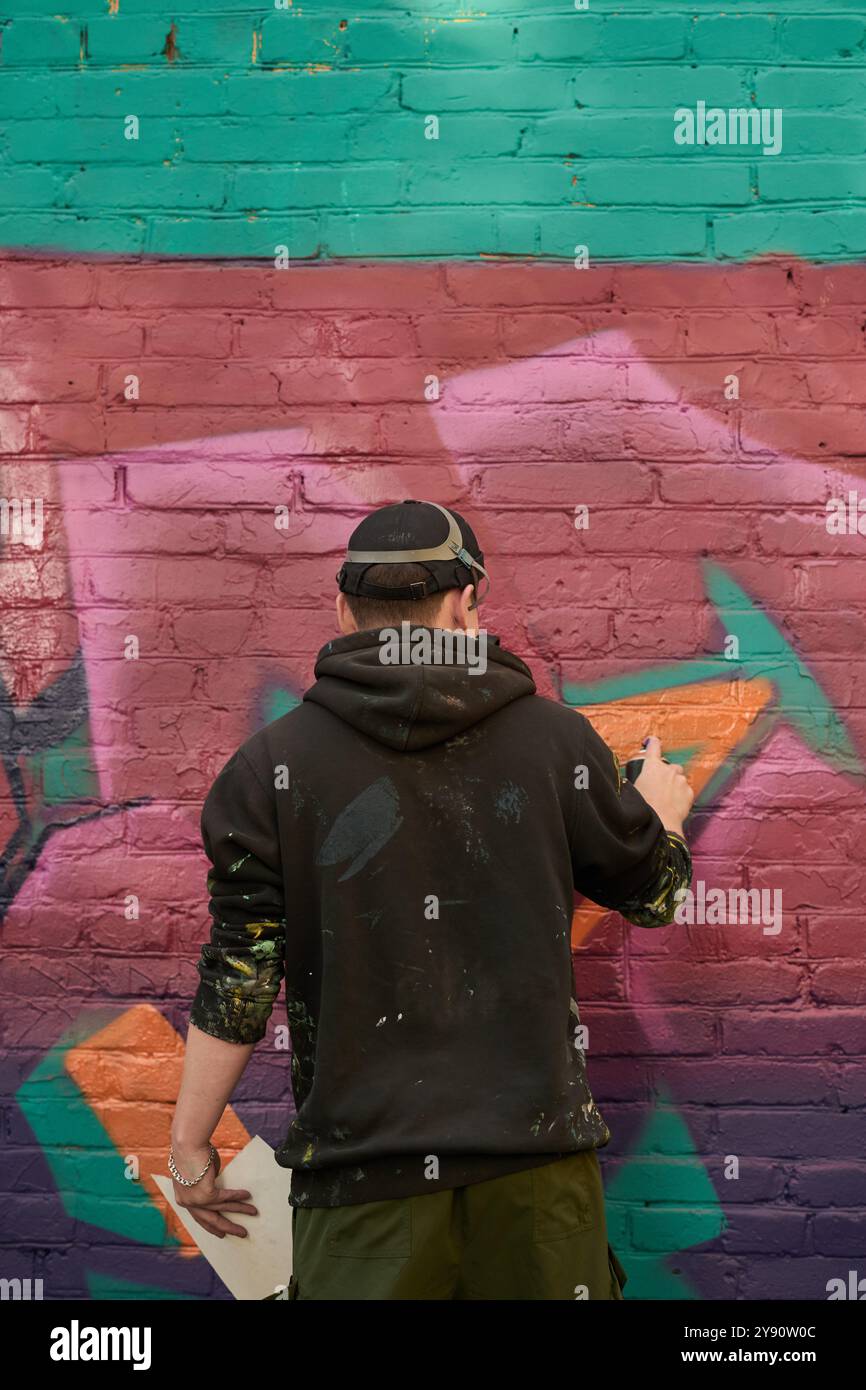 rear view of skilled guy with spray paint applying it on brick building ...