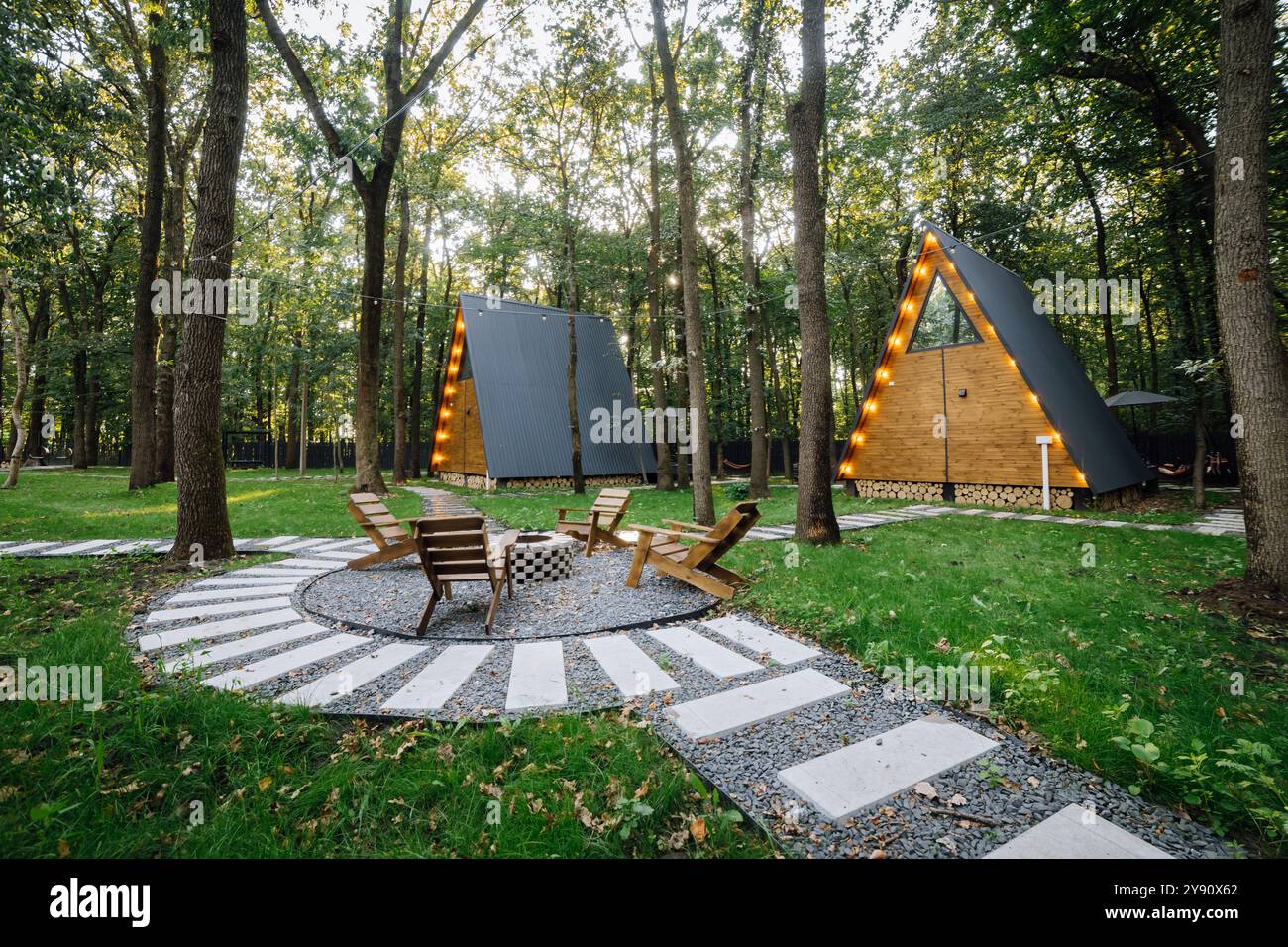 Modern wooden A-frame cabins in forest with outdoor seating and fire ...