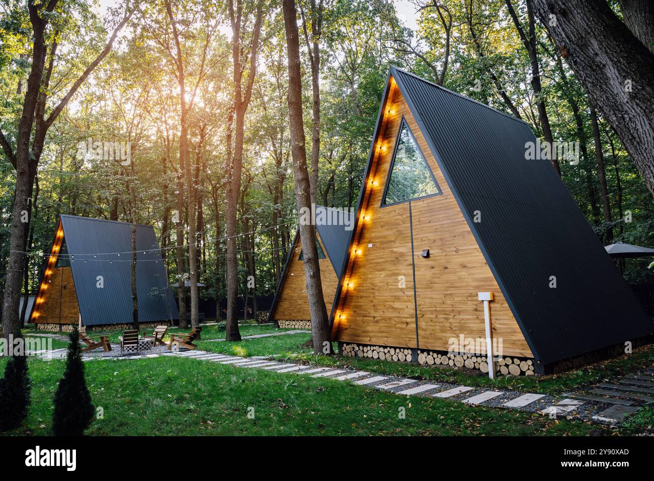 Cozy wooden A-frame cabins in forest with sunlight and outdoor seating ...