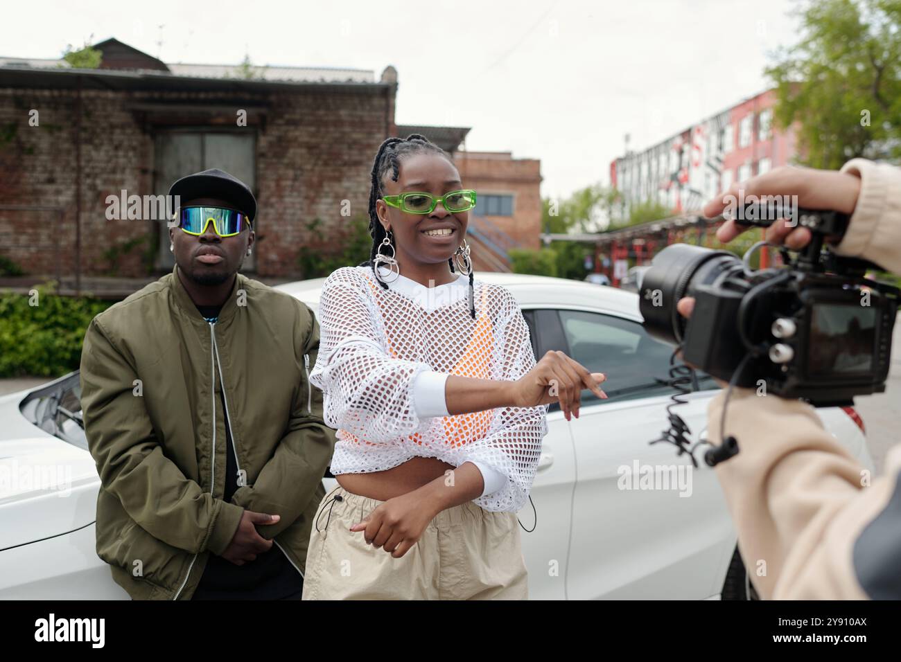 Two people standing outdoors behind parked car, one interviewing other ...