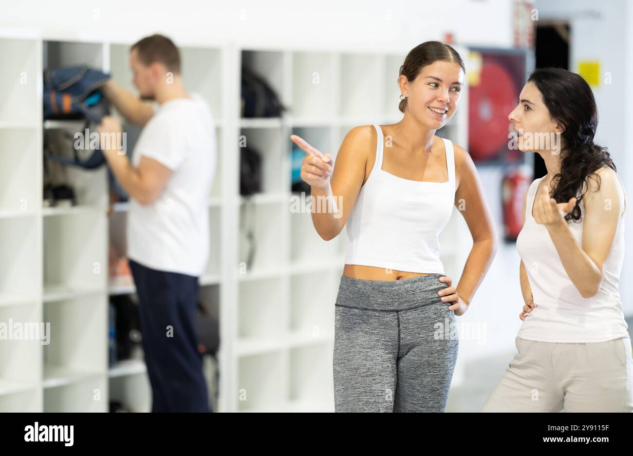 Two female climbers laughing and sharing stories in climbing gym locker room after exciting ...