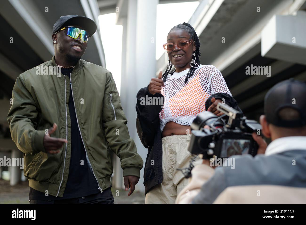 Two young adults standing under an overpass with a cameraman capturing ...