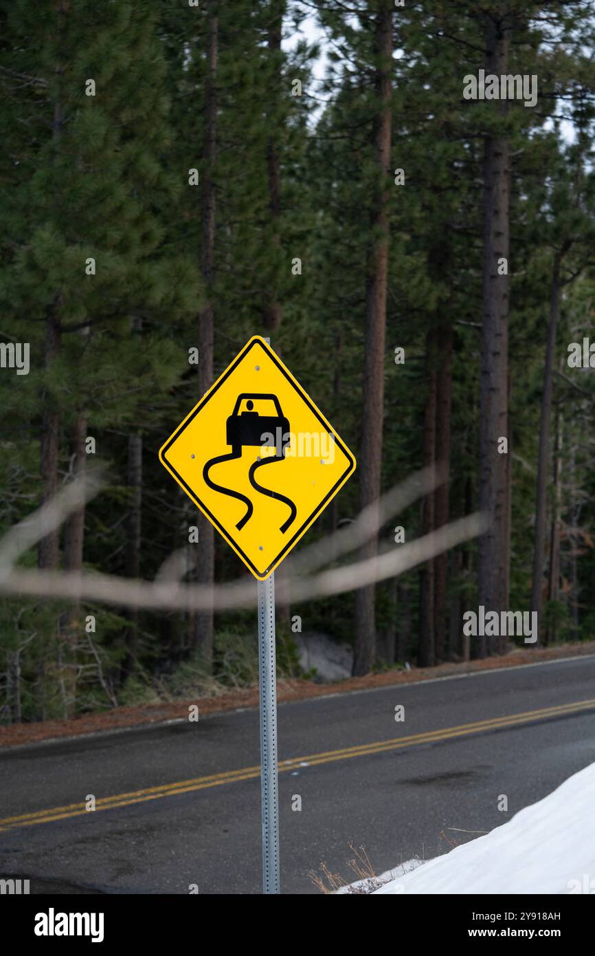 Slippery when wet road sign with forest and road backdrop. Snow and ...