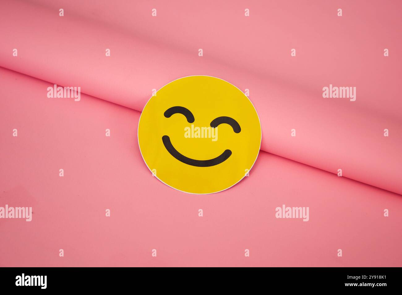 A pink smiling emoji tucked behind a pink background Stock Photo - Alamy