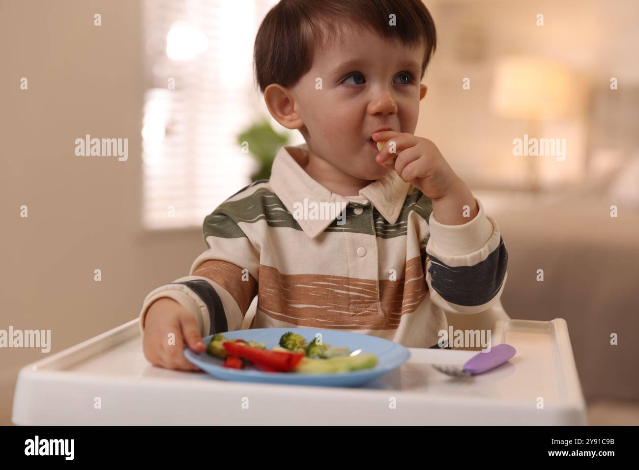 Cute little baby eating healthy food in high chair at home Stock Photo ...