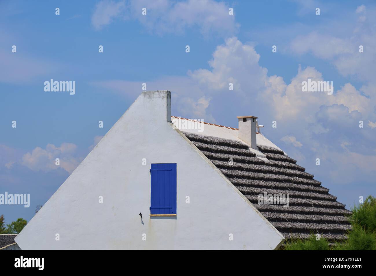 White cottage with thatched roof and round window under a blue sky ...