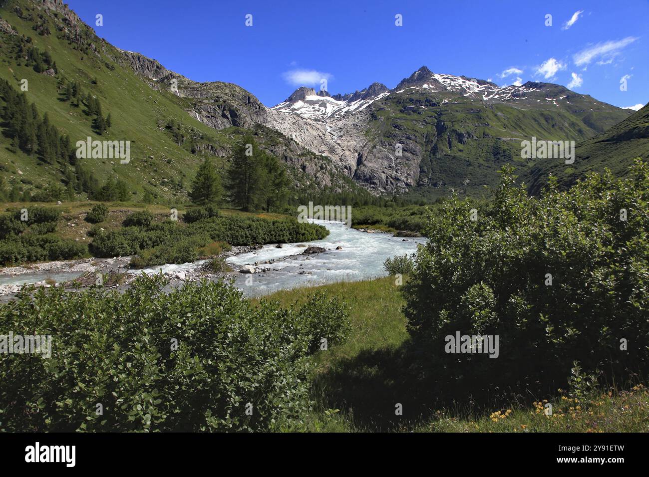 A clear river flows through a green valley, surrounded by wooded ...