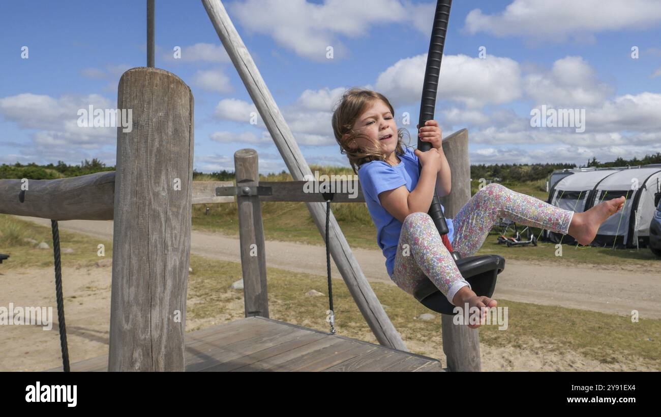 A child happily jumps on a zip wire in a wide, sunny playground setting ...