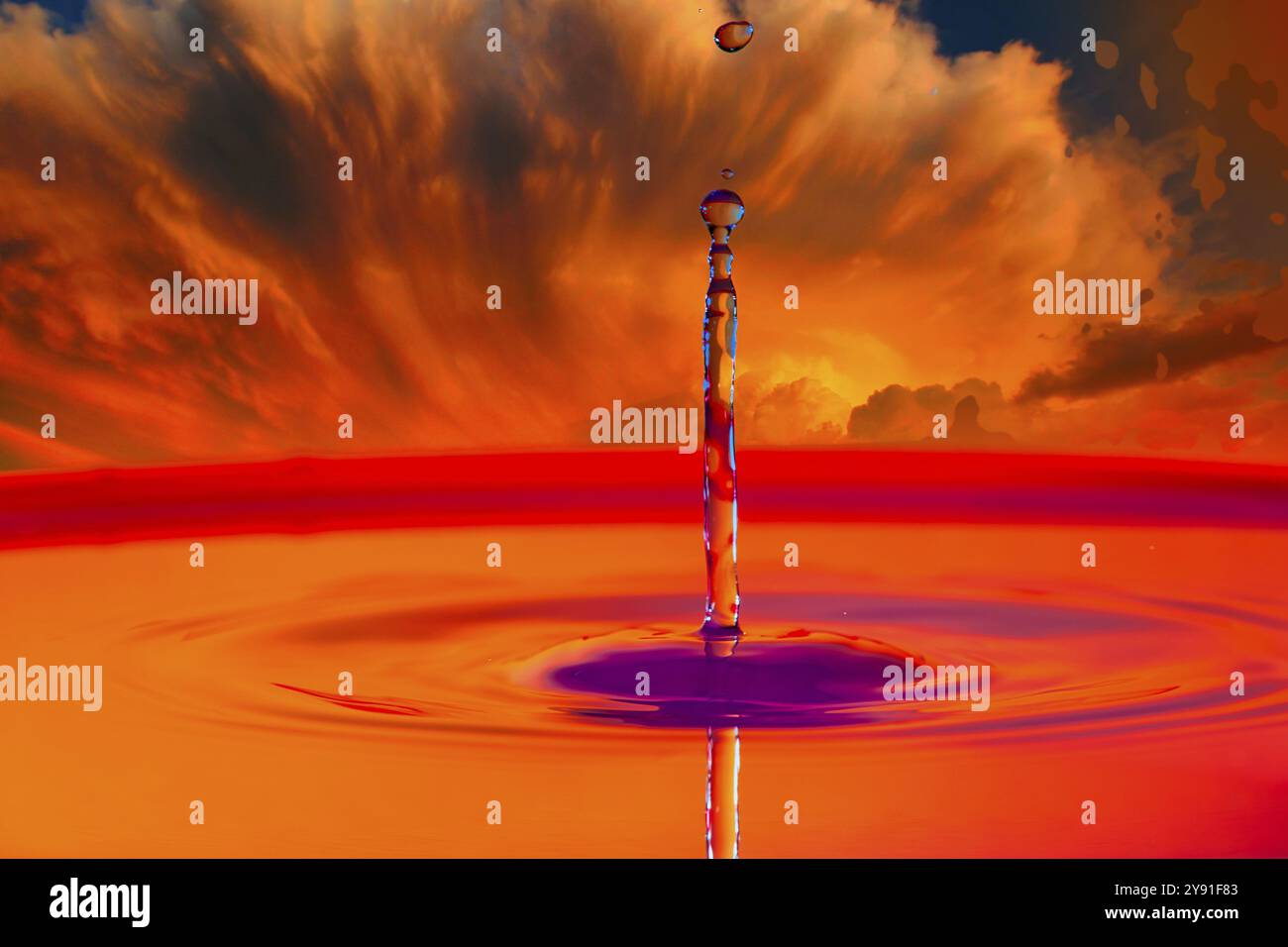 A falling drop of water in front of a rich, colourful sunset sky with ...