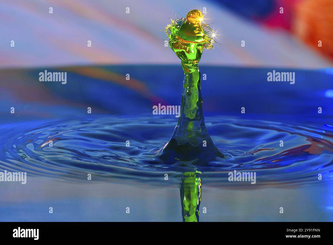 A drop of water in bright green creates a lively splashing movement on ...