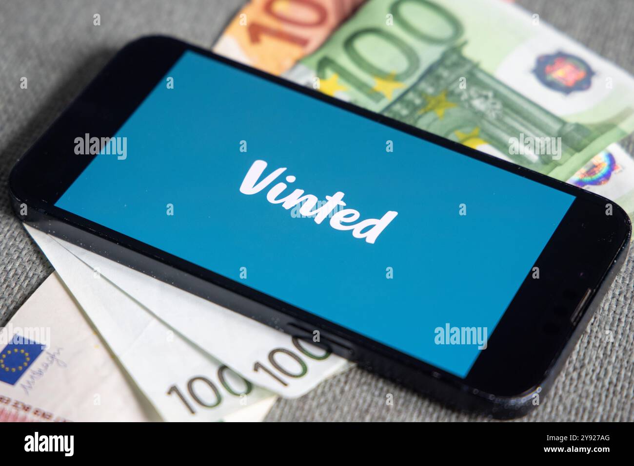 Iphone with Vinted logo on screen on stack of money. Vinted is a Lithuanian online marketplace ...