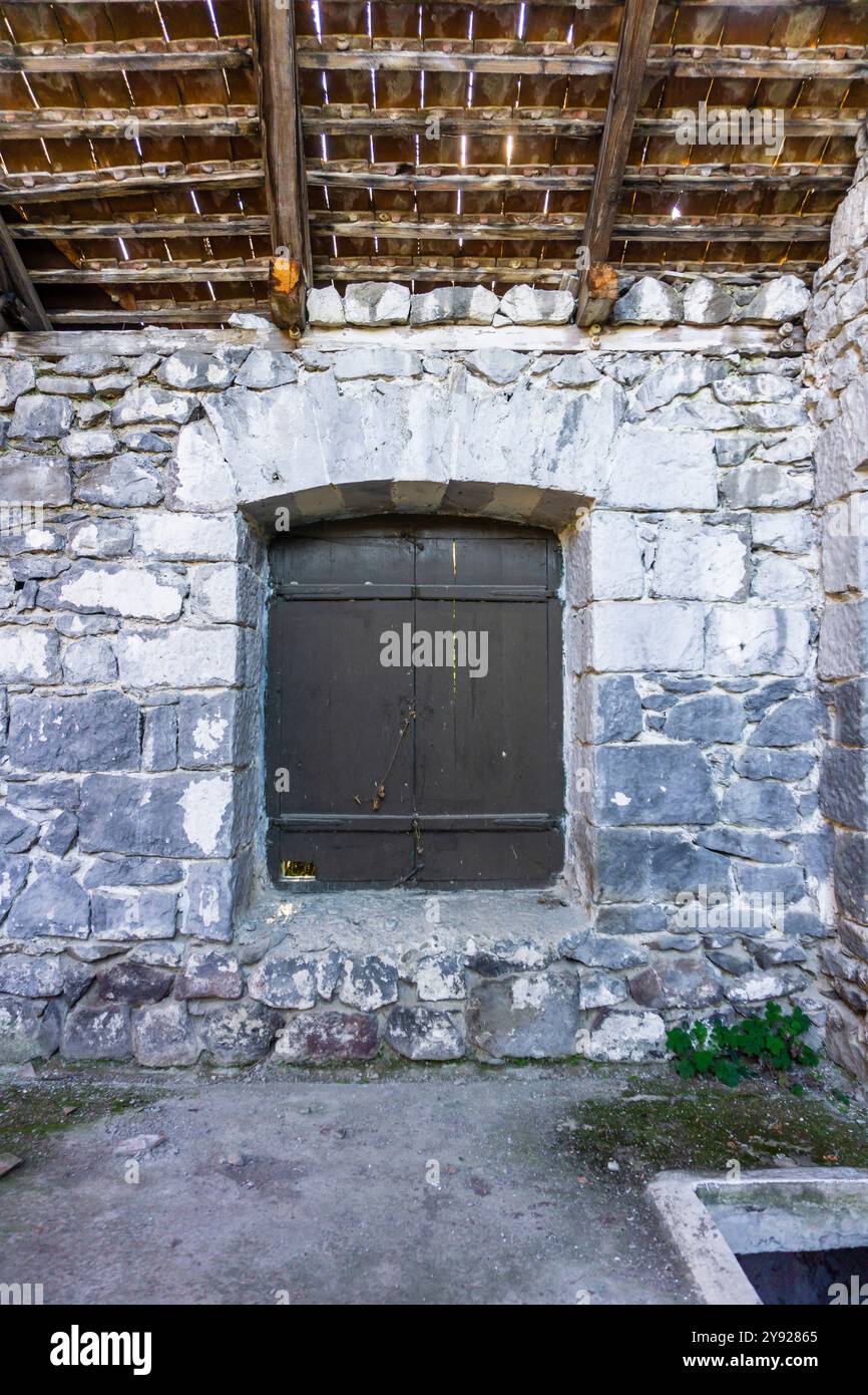 Wooden brown window without glass in a thick wall of gray stones ...