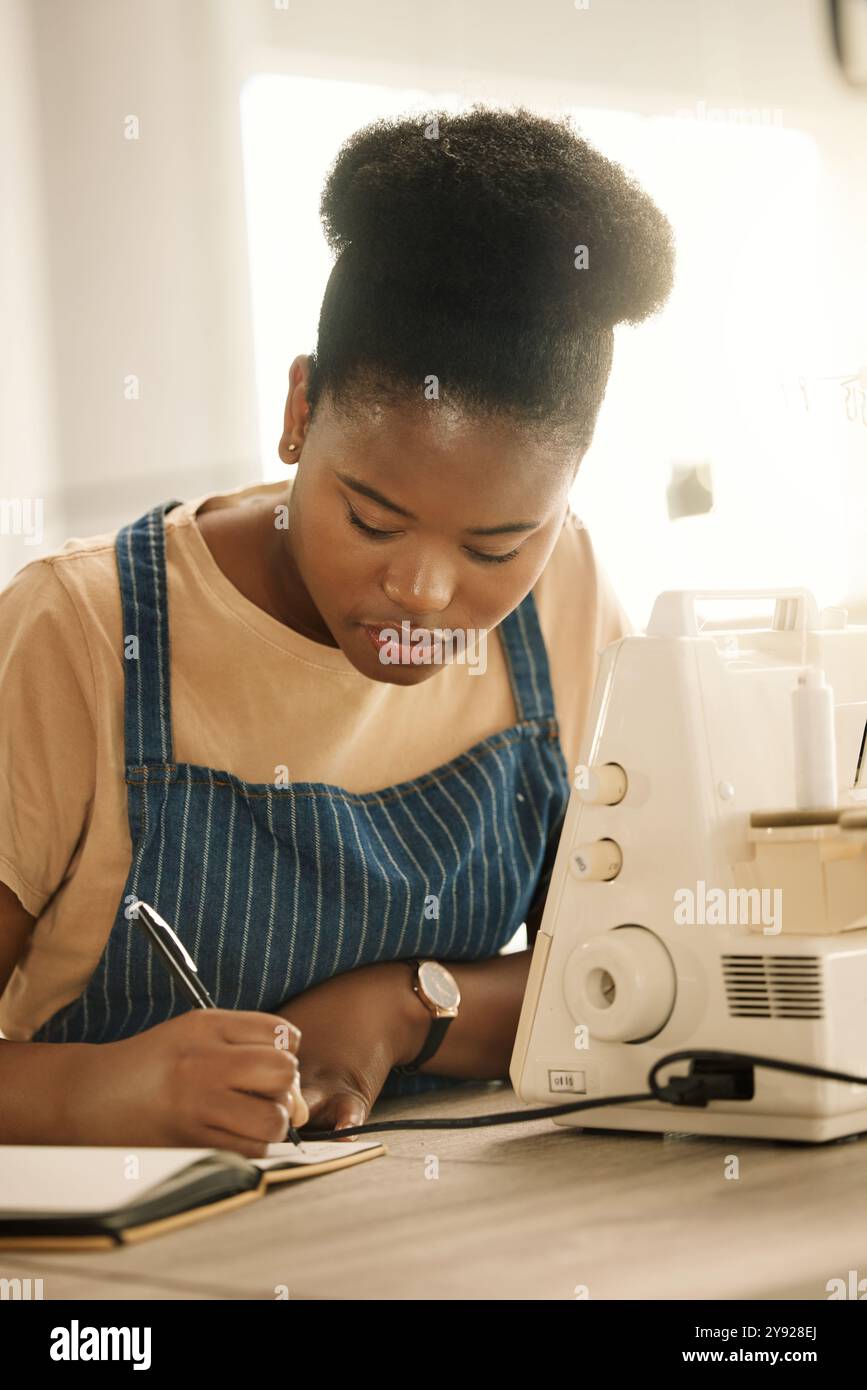 Black woman, fashion student and writing on journal with sewing machine ...