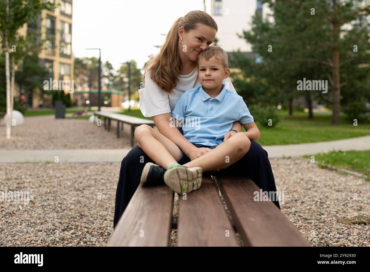 A mother and son share a joyful moment on a bench in a sunny park ...