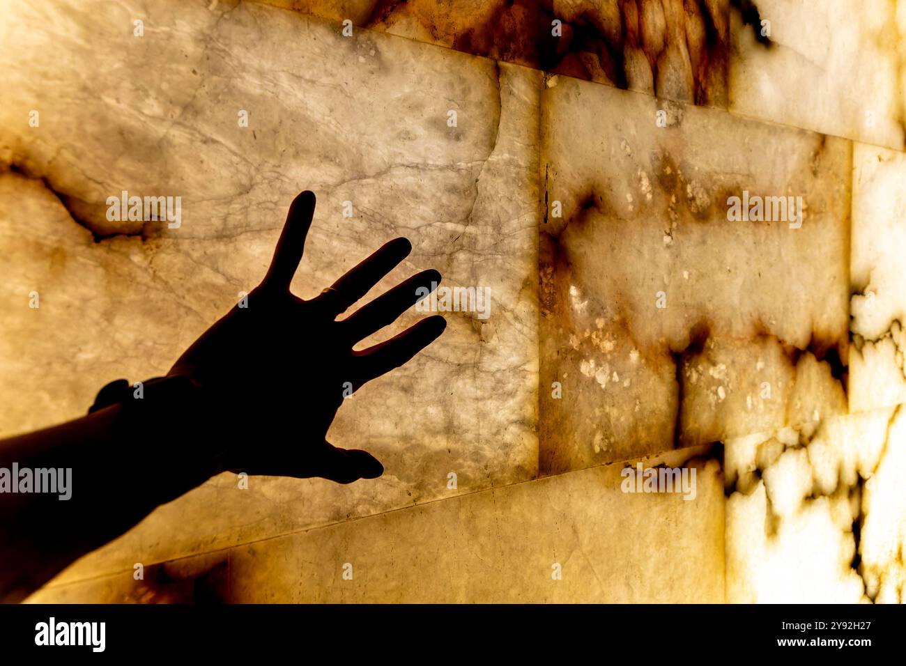 A hand is reaching out to touch a wall with a stone surface. The hand ...