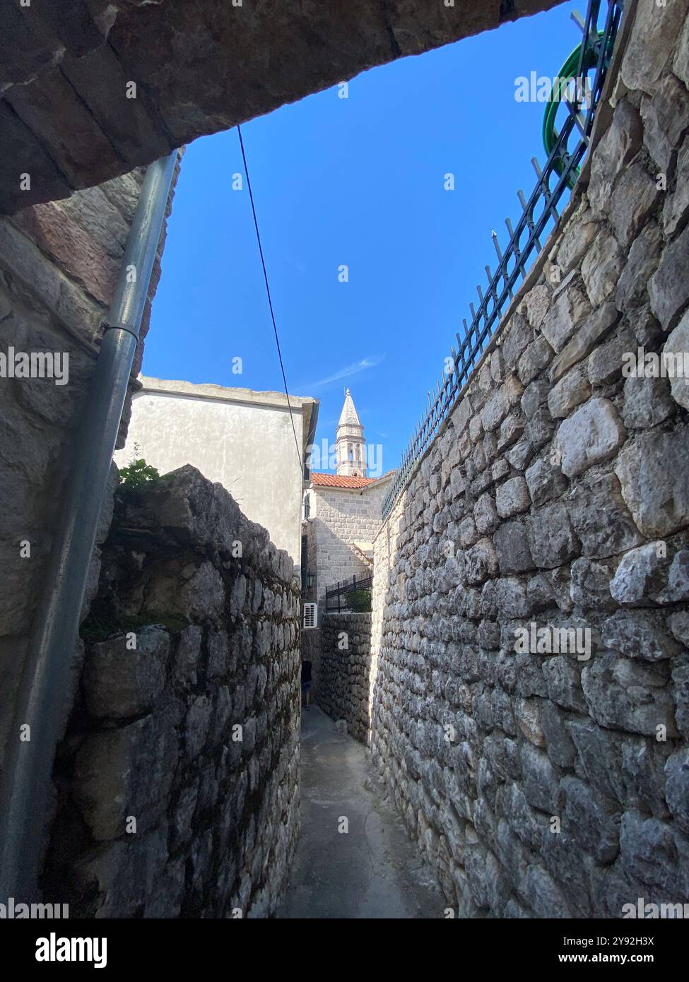 Narrow stone alleyway leading to a historic tower against a clear blue ...