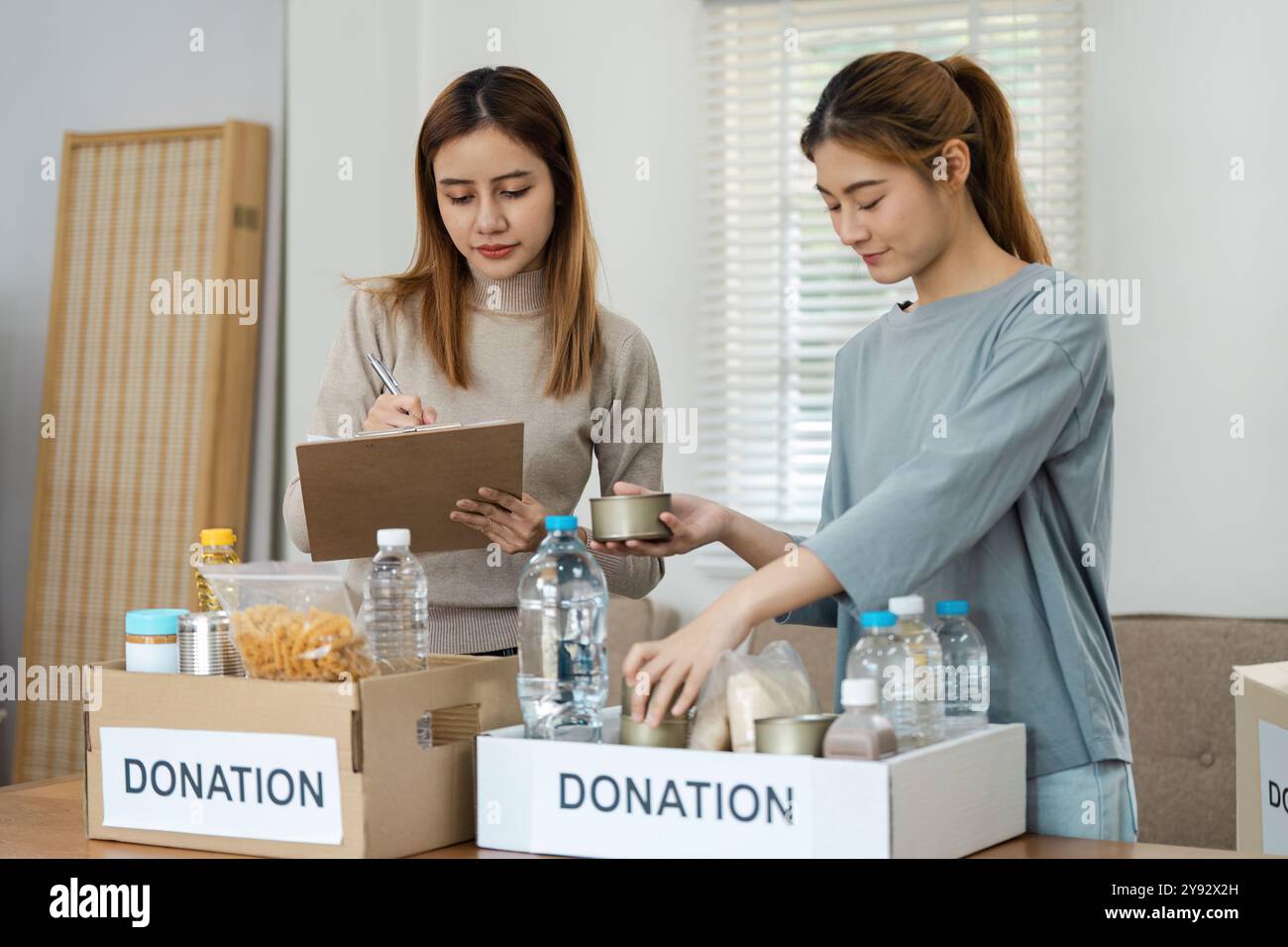 Two Women Organizing Donation Boxes with Food and Water in a Bright ...