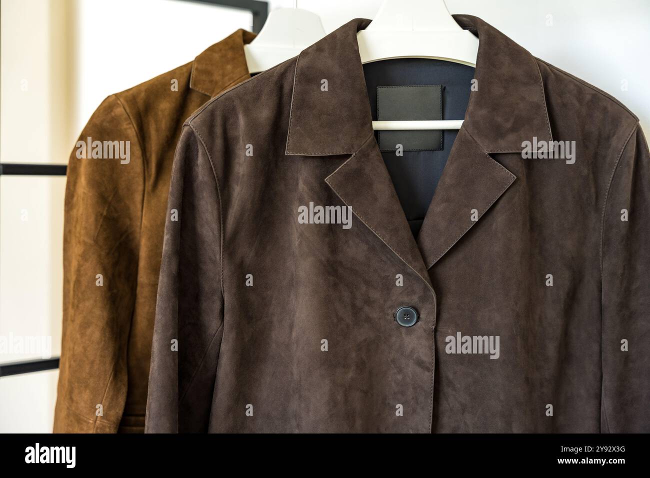 Two brown leather suede jackets of different shades hanging on a hanger ...