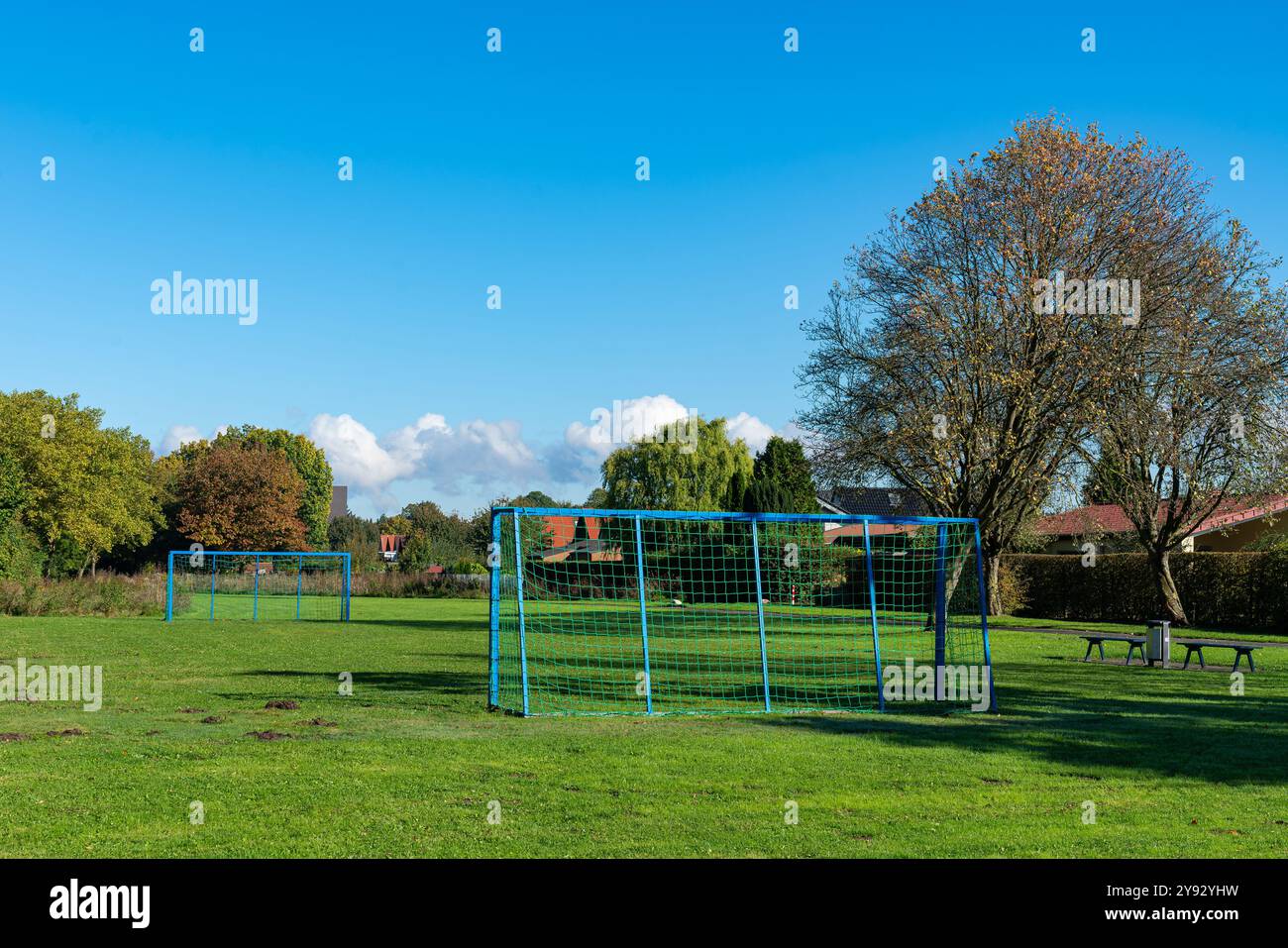 A bright, sunny day in a local park features two soccer goals set up on ...