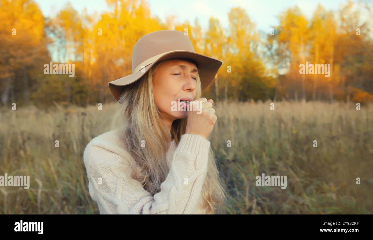 Cold and health, sick mature woman coughing outdoors in autumn park ...