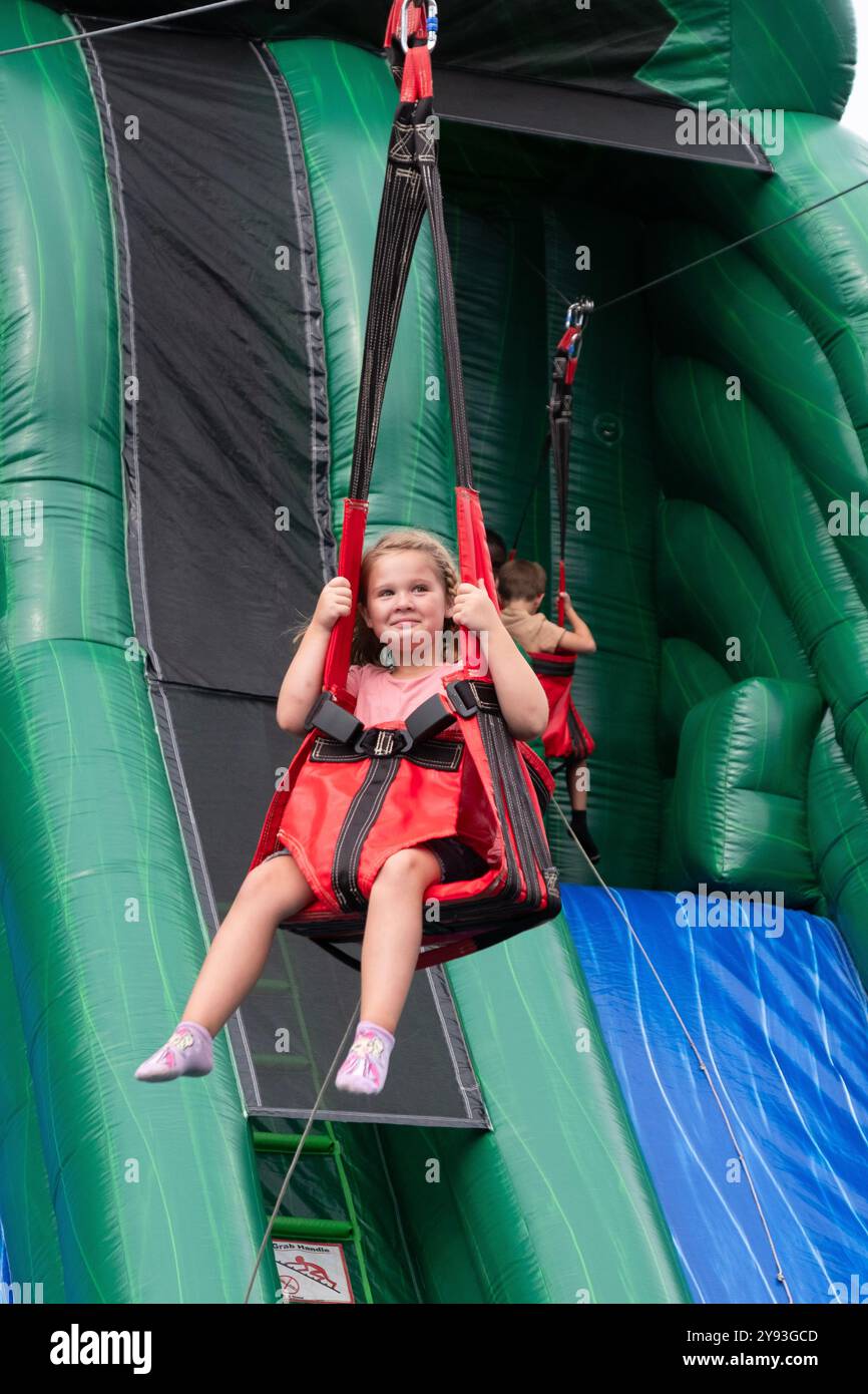 A very happy young shoeless girl rides the Amazon Zip Line at the 2024 ...