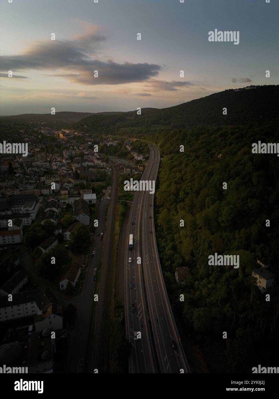 Aerial view of a highway curving through a lush green forest and a town ...