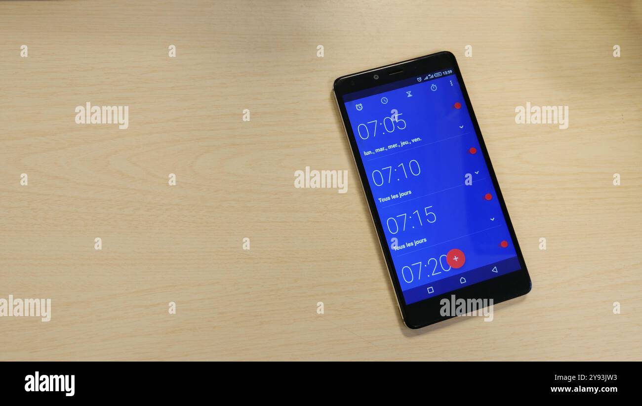 A smartphone displaying multiple alarm times on a wooden surface ...