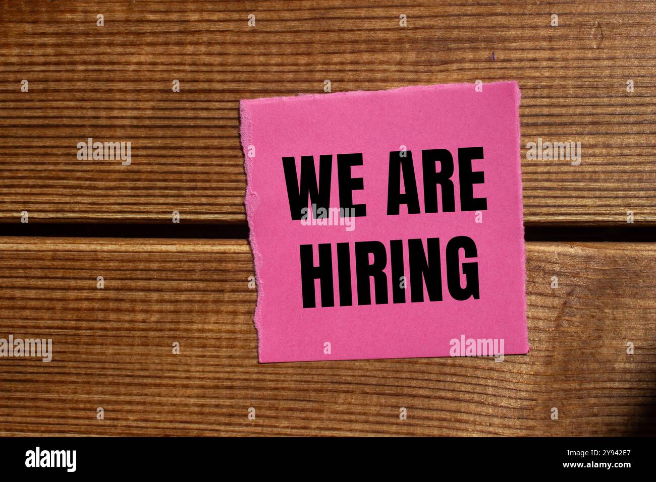 We are hiring message written on ripped torn pink paper piece with wooden background. Conceptual ...