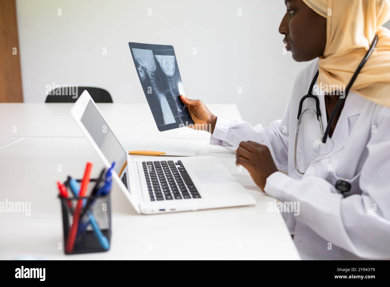 A professional black female doctor in a hijab examines an X-ray film at ...