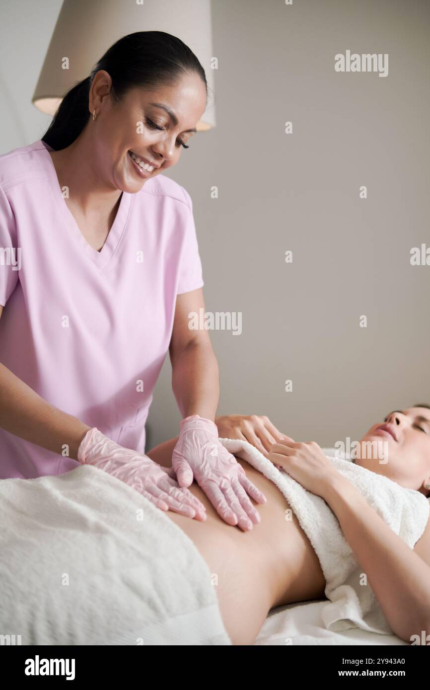 A professional female massage therapist in a pink uniform is giving a ...