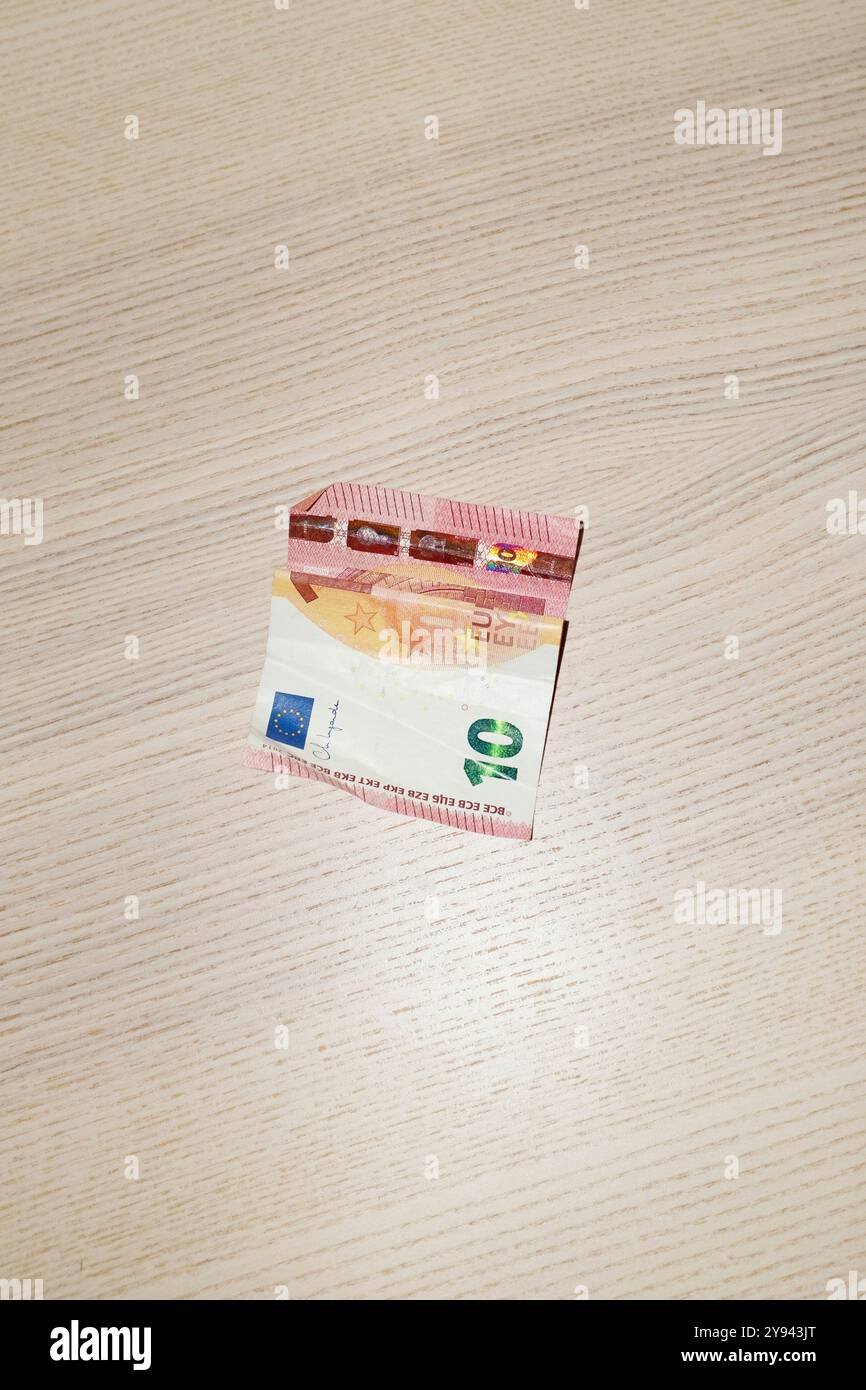 A 10 euro banknote is positioned on a pale textured wooden desk ...