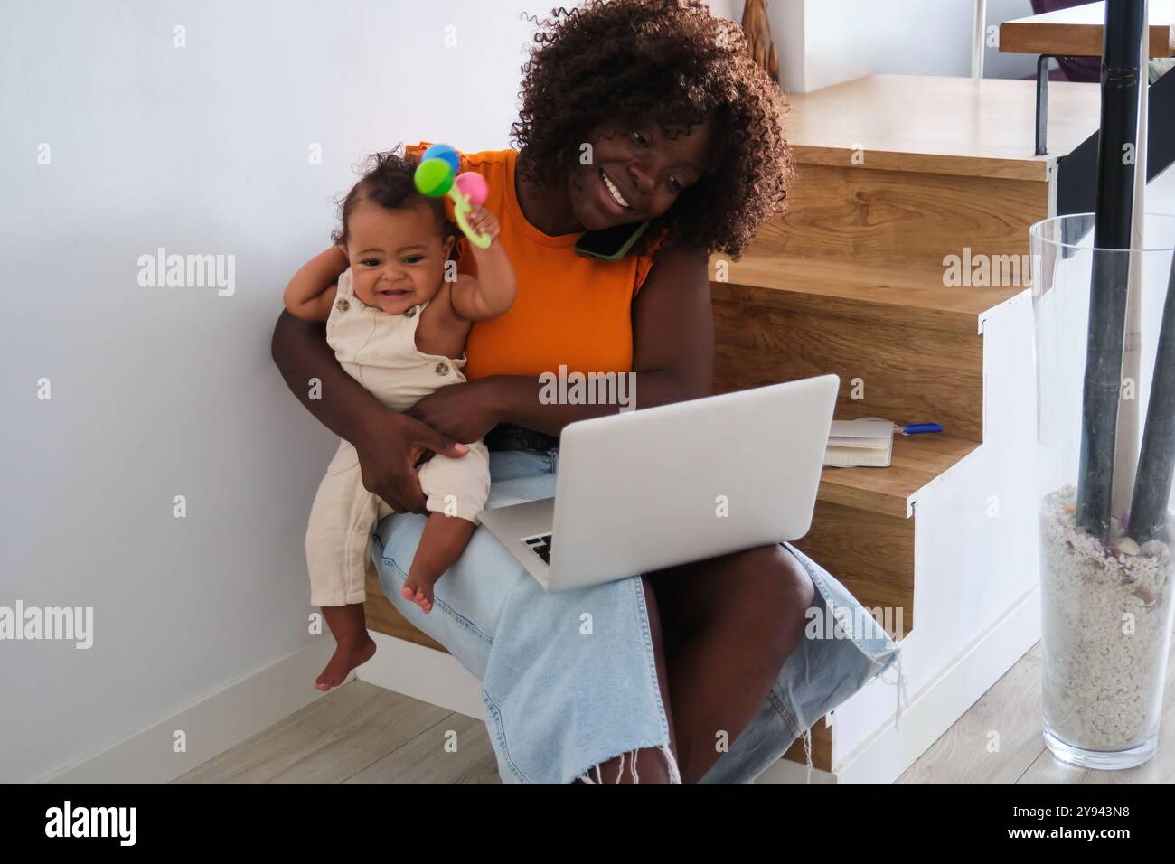 A cheerful African mother sitting on stairs holds her baby girl while ...