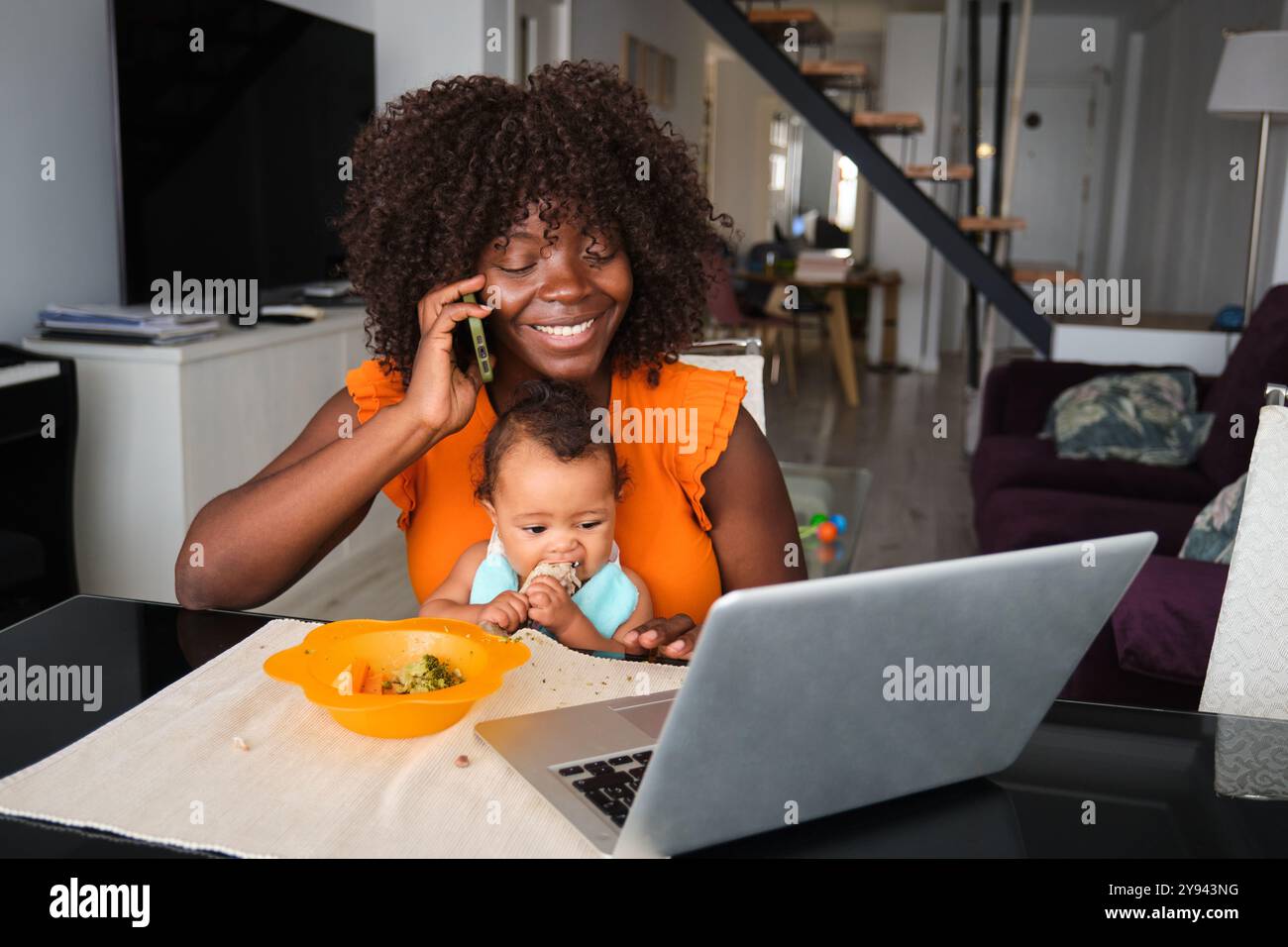 A cheerful Black African mother engages in multitasking, talking on the ...