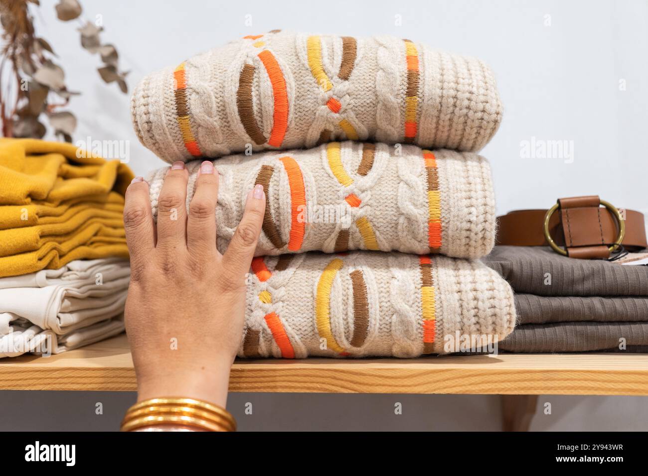 A person's hand touches stacked cozy knit sweaters in warm earth tones ...