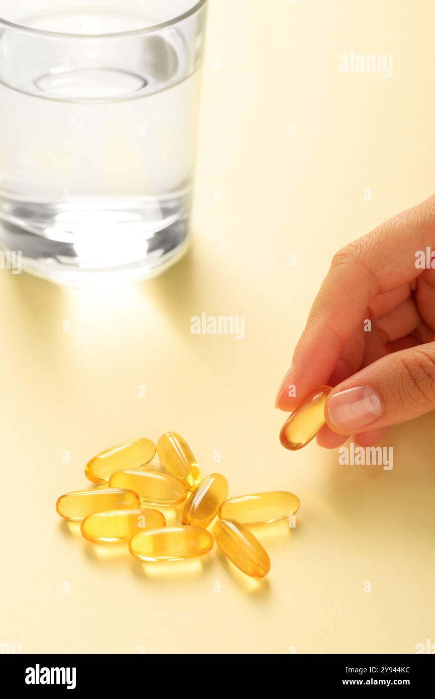Hand picks up one omega-3 capsule from a handful of similar capsules ...