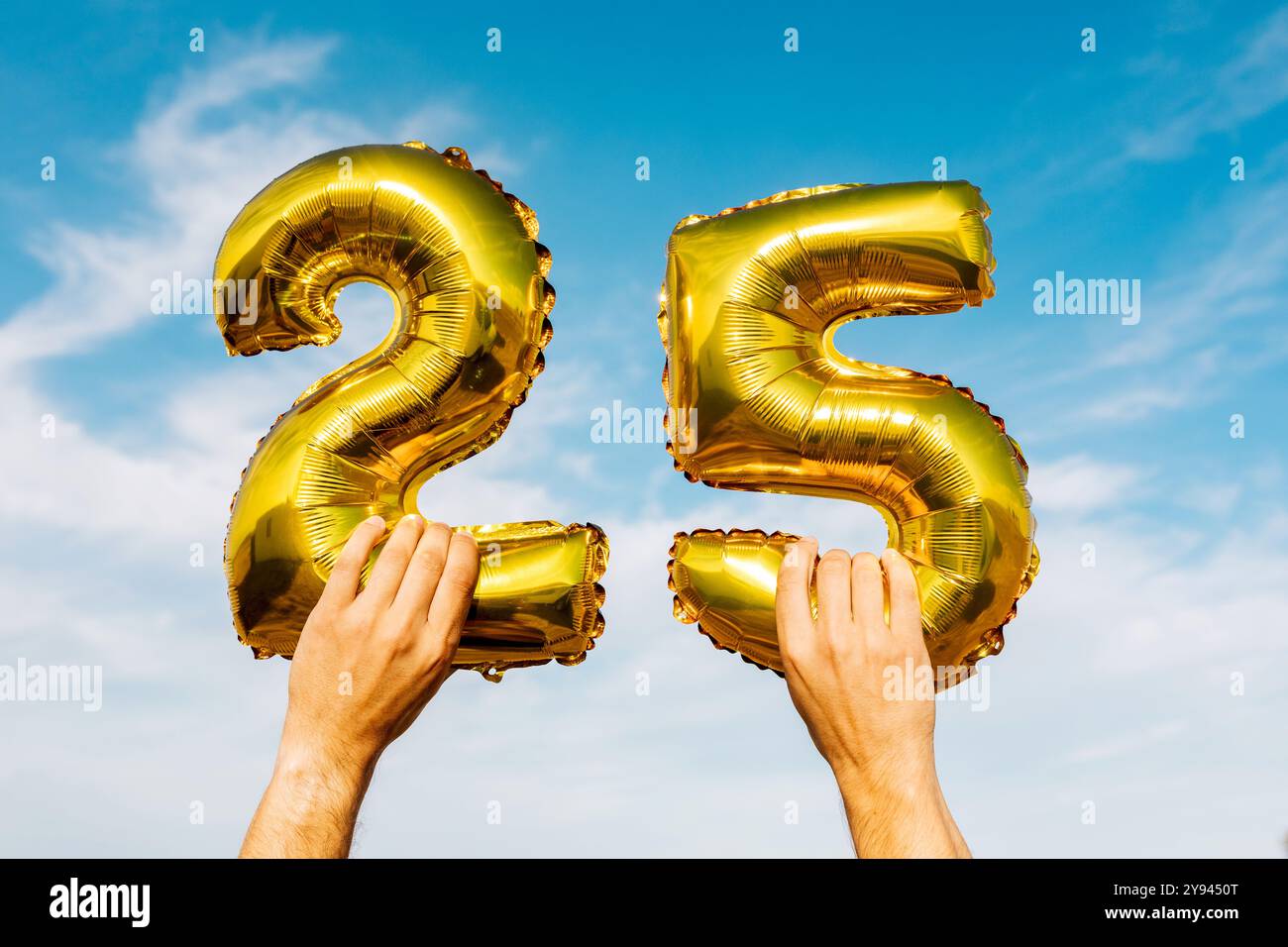 Cropped view of hands holding shiny gold number 25 balloons, with a ...