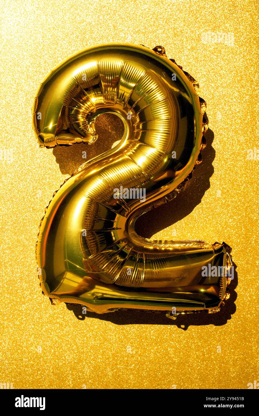 A shiny golden balloon shaped like the number 2 set against a sparkling ...