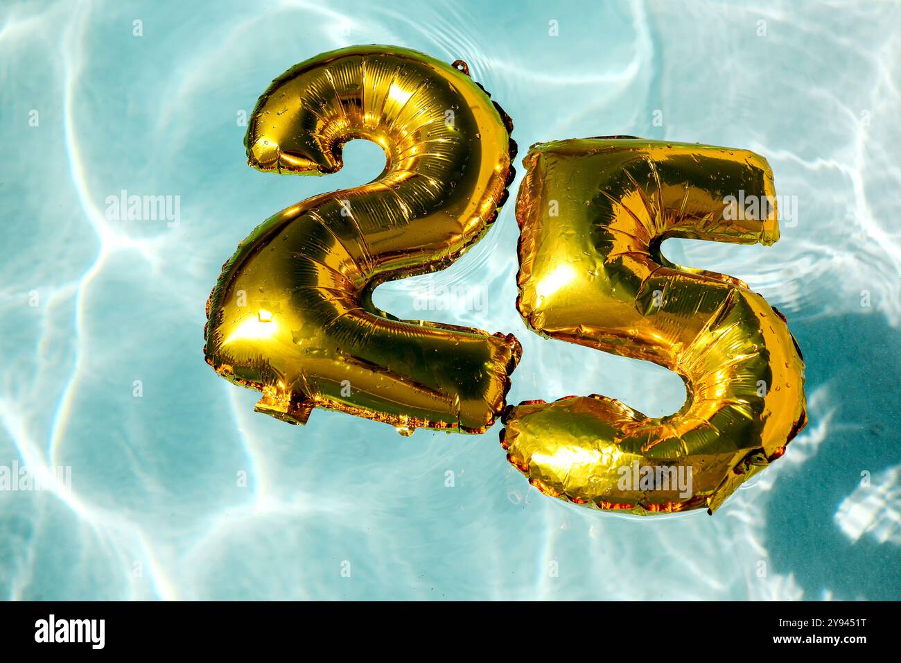 Golden number 25 balloons reflect the sunlight while floating on a pool ...