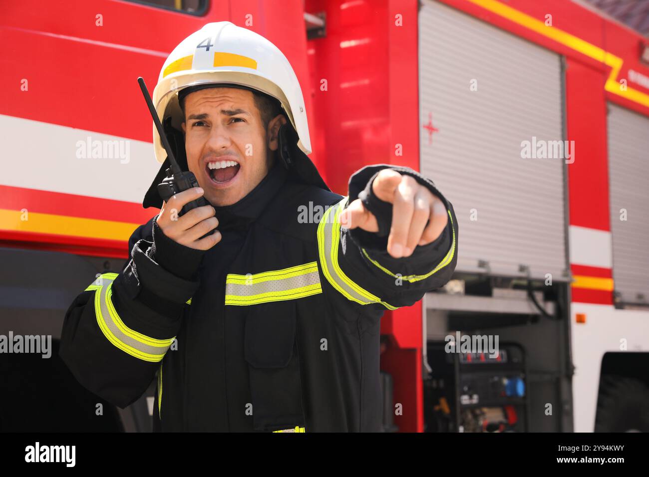 Firefighter in uniform using portable radio set near fire truck ...