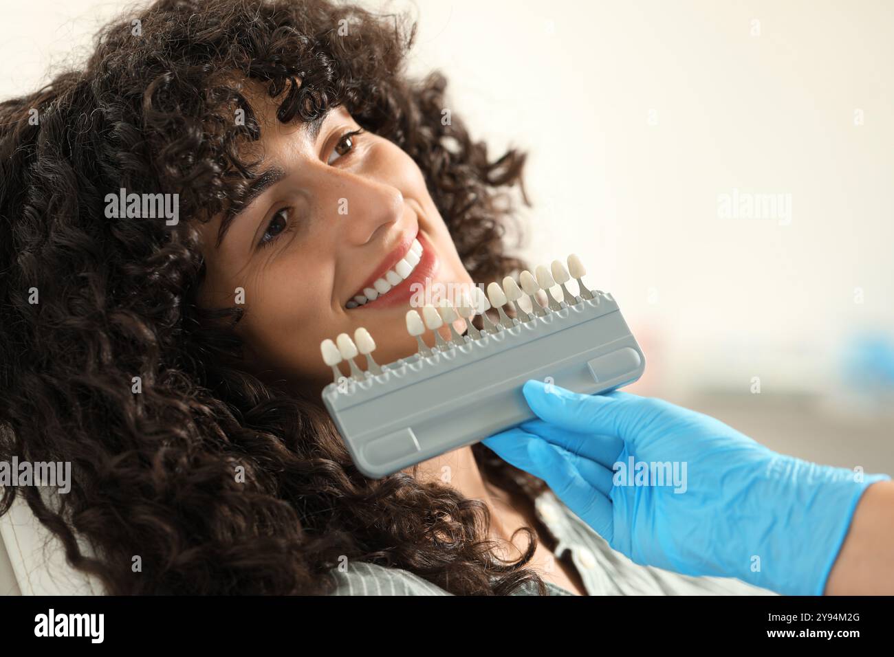 Doctor checking young woman's teeth color in clinic, closeup. Dental ...