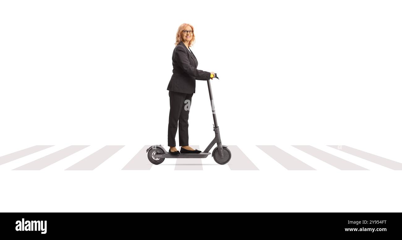 Middle aged woman riding an electric scooter at a pedestrian zebra ...