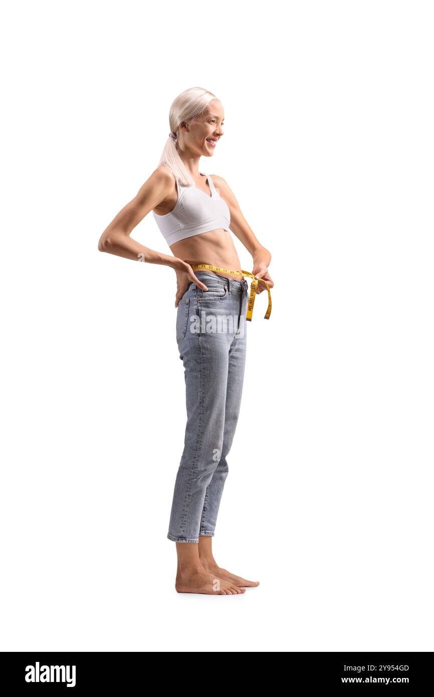 Young slim woman in jeans and crop top measuring waste with a tape ...