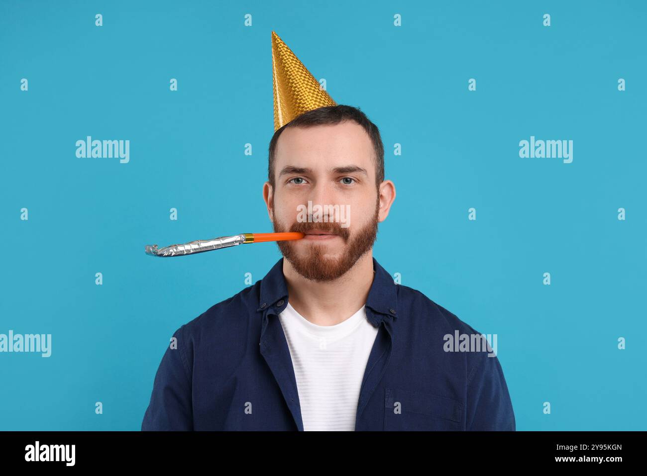 Man in party hat with blower on light blue background Stock Photo - Alamy