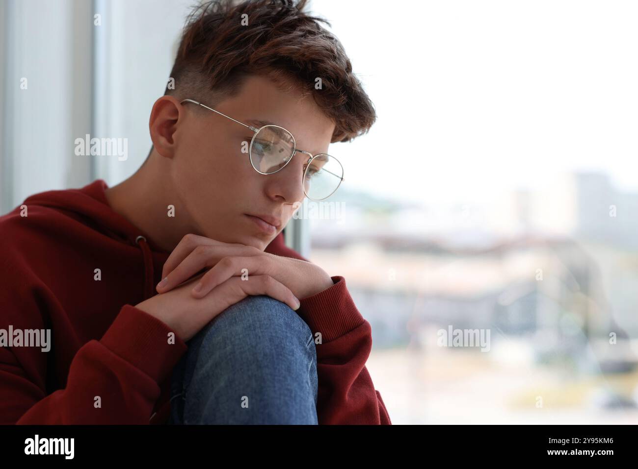 Loneliness concept. Sad teenage boy near window indoors, space for text ...