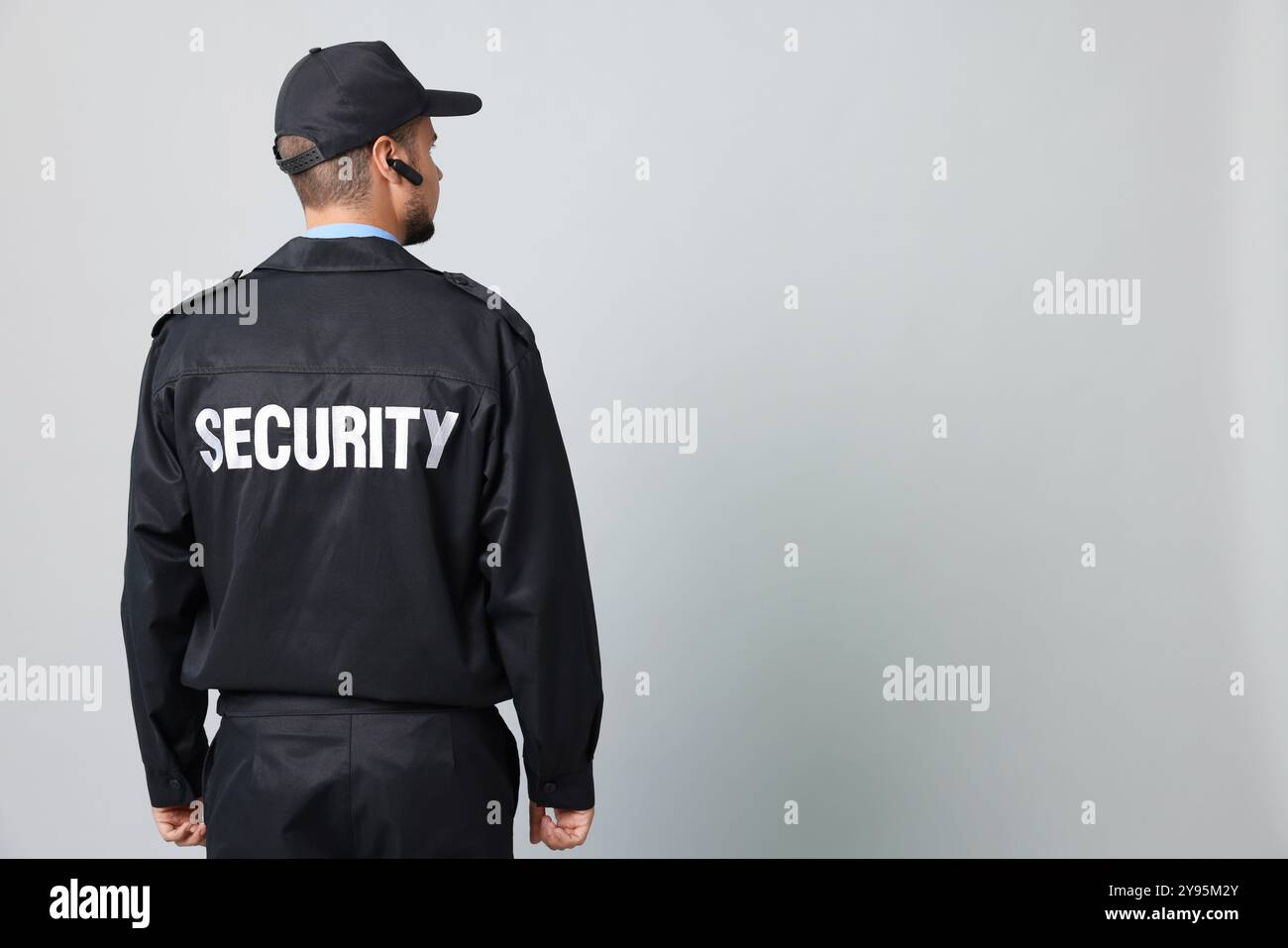 Security guard in uniform with earpiece on grey background, back view ...